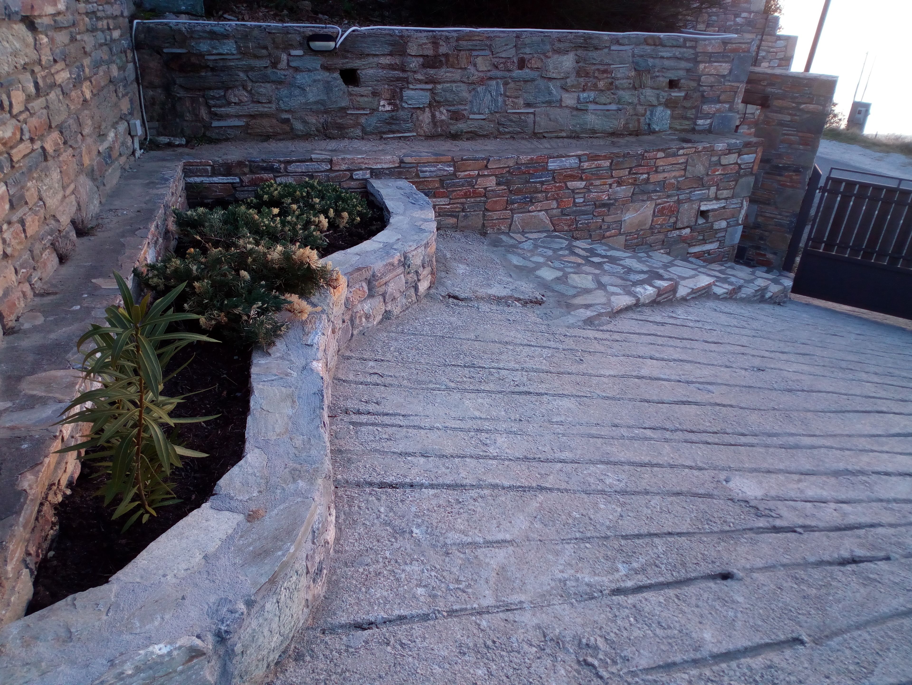 Caminho de pedra que leva a um portão com muro de pedra e um pequeno jardim com plantas.