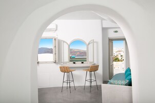Quarto com duas cadeiras de vime, janela com vista para montanhas e uma parede branca.