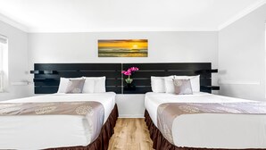 Quarto de hotel com duas camas, piso de madeira, cabeceira preta e uma pintura de pôr do sol na parede.