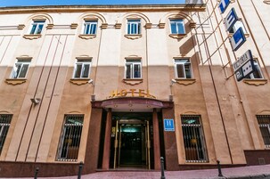 Entrada de hotel com fachada clássica, grandes janelas e sinalização indicando área de estacionamento.