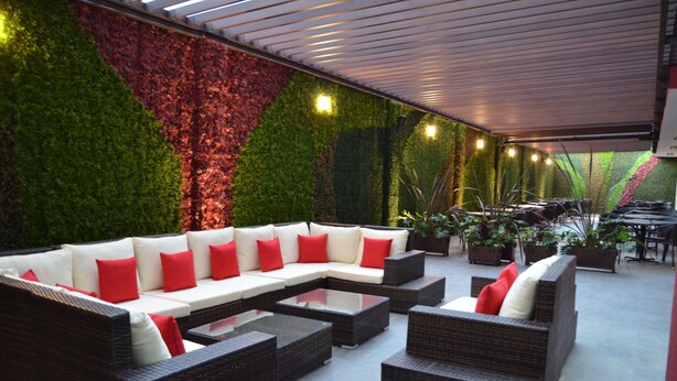 Uma área de estar moderna ao ar livre, com sofá modular e móveis de vime, rodeada por um muro verde exuberante e plantas em vasos.