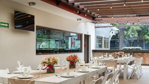 Um restaurante com várias mesas de jantar preparadas para os clientes, uma grande janela com vista para o exterior e uma televisão na parede.