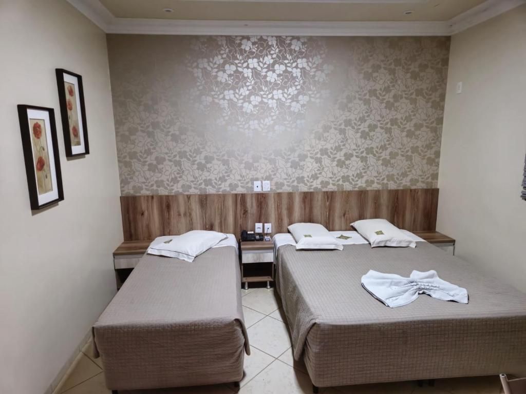 Quarto de hotel com duas camas de solteiro, cabeceira de madeira e uma parede decorativa.