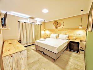 Quarto de hotel com cama, mesas de cabeceira, televisão, cortinas e uma obra de arte pendurada na parede.