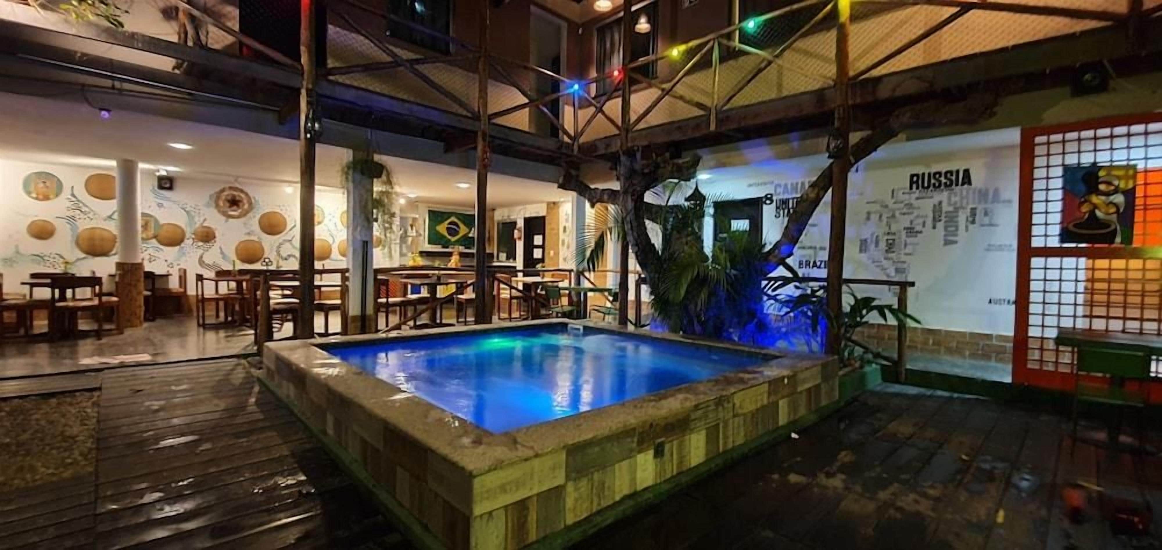 Piscina interna com deck de madeira ao redor, área de bar com assentos e parede com mapa e bandeiras.