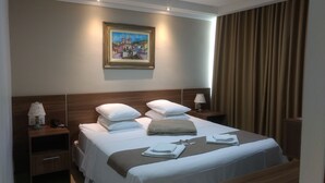 Quarto de hotel com cama bem arrumada, um quadro na parede e uma janela com cortinas.