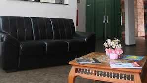 Um hall moderno com um sofá de couro preto, uma mesa de centro de madeira com revistas, uma planta em vaso e um lustre decorativo.