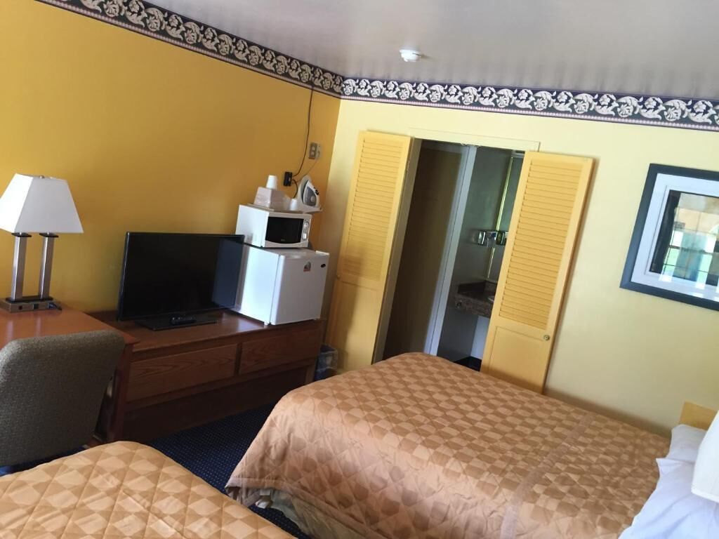 Quarto de hotel com uma cama, uma escrivaninha com televisão, micro-ondas e uma porta para o banheiro.