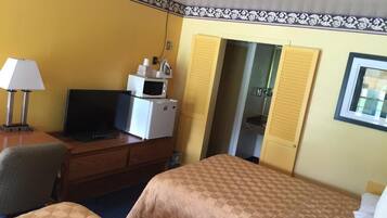 Quarto de hotel com uma cama, uma escrivaninha com televisão, micro-ondas e uma porta para o banheiro.