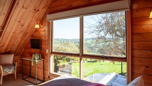 Quarto aconchegante com uma janela grande, uma cama, uma cadeira e uma mesinha com uma planta.