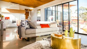 Uma sala de estar moderna com um sofá, uma mesa de centro redonda dourada e uma janela grande com vista para o exterior.