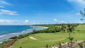 Um campo de golfe com vista para o oceano e um edifício ao longe.