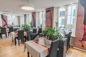 Interior moderno de restaurante, com piso de madeira, cadeiras pretas e mesas preparadas para refeições.