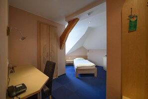 Quarto de hotel com escrivaninha, cadeira, cama e mesa de cabeceira.