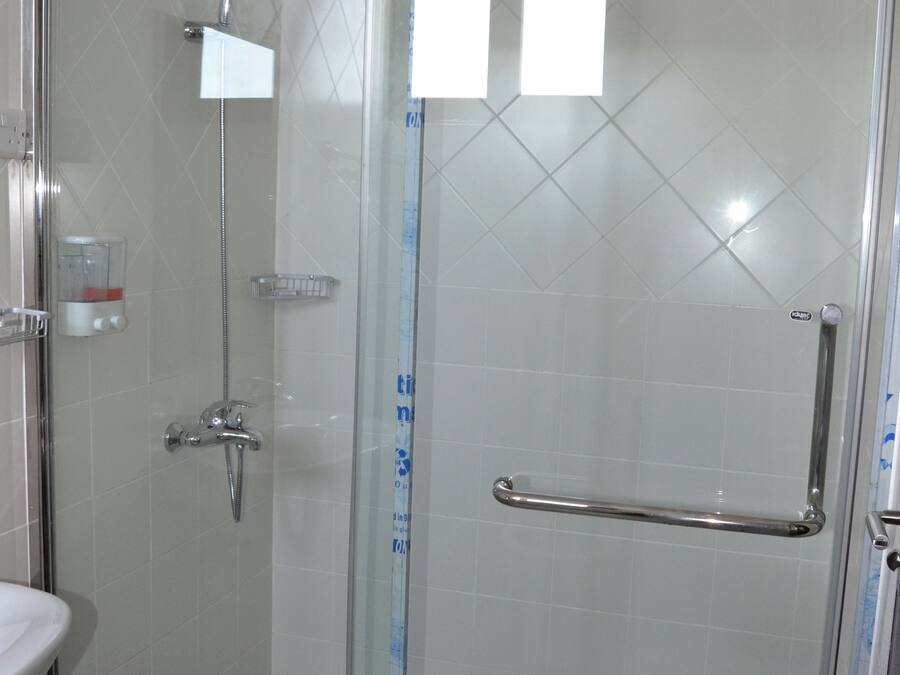 Divisória de chuveiro envidraçada com barra de apoio, chuveiro e um pequeno prateleira.