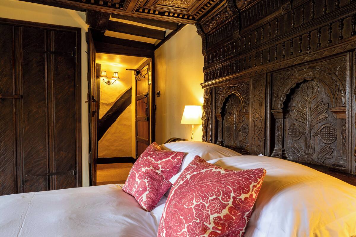 Um quarto com uma cama, cabeceira de madeira, escada e uma luminária.