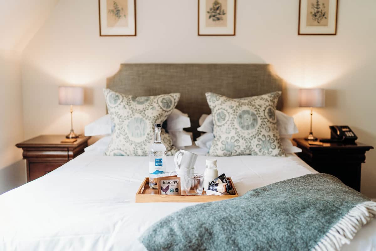 Cama bem arrumada com um bandejão de artigos de higiene pessoal e uma garrafa de vinho South Downs.