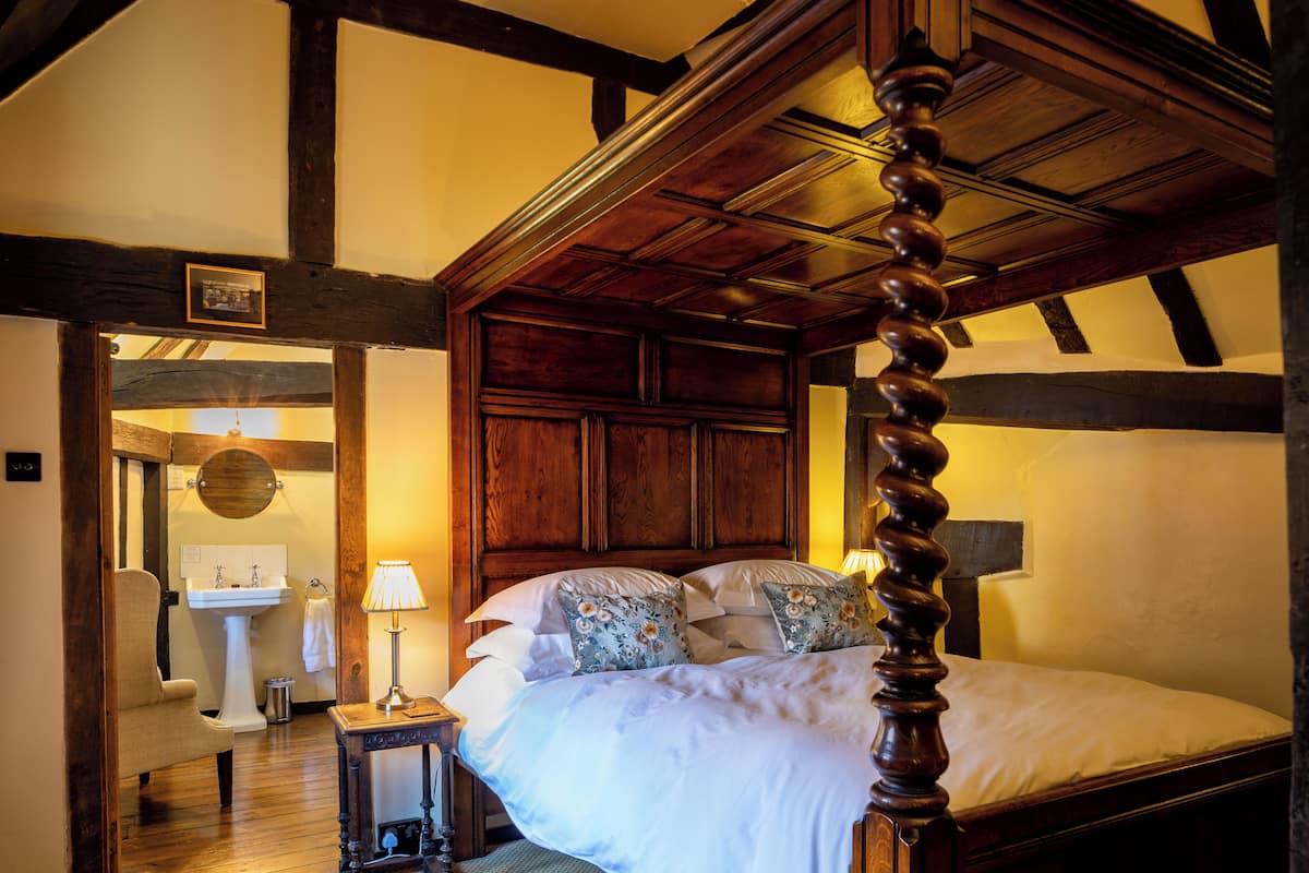 Quarto tradicional com cama de dossel, vigas de madeira e design clássico.