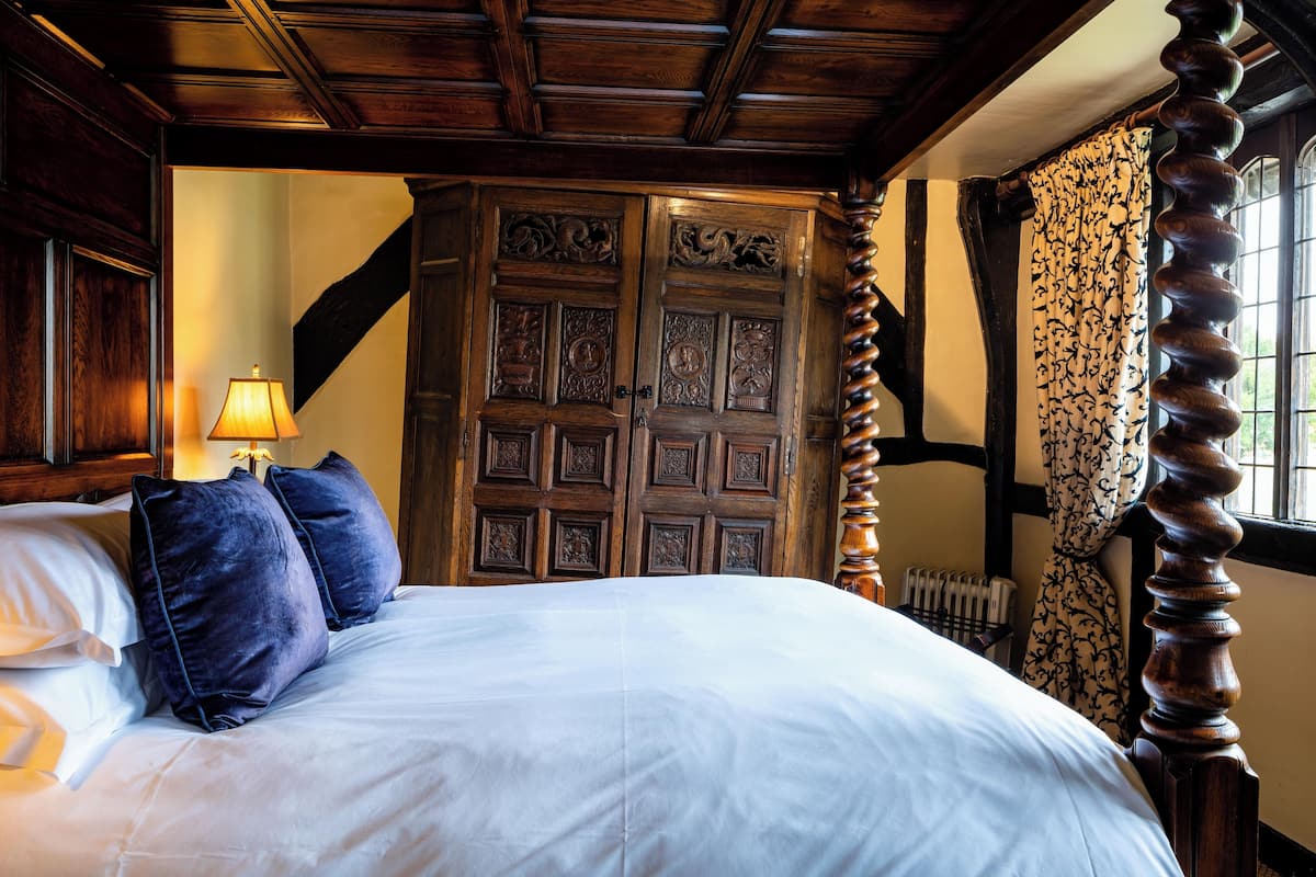 Quarto tradicional com uma cama grande, porta de madeira com detalhes entalhados e janela com cortinas estampadas.
