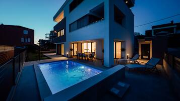 Uma casa moderna com dois andares, piscina, área de estar externa e um pátio bem iluminado.
