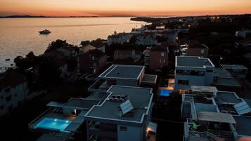 Zona residencial com edifícios modernos, piscina e vista para o mar ao pôr do sol.