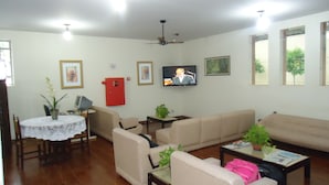 Uma sala de estar com televisão, sofá, cadeiras, uma mesa e um armário vermelho.