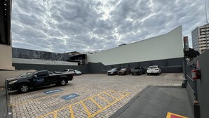 Uma área de estacionamento com vários carros, um edifício com fachada branca e uma vaga de estacionamento para deficientes azuis.