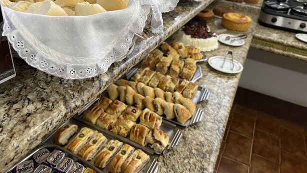 Buffet com diversos produtos de panificação, incluindo pães, doces e tortas.