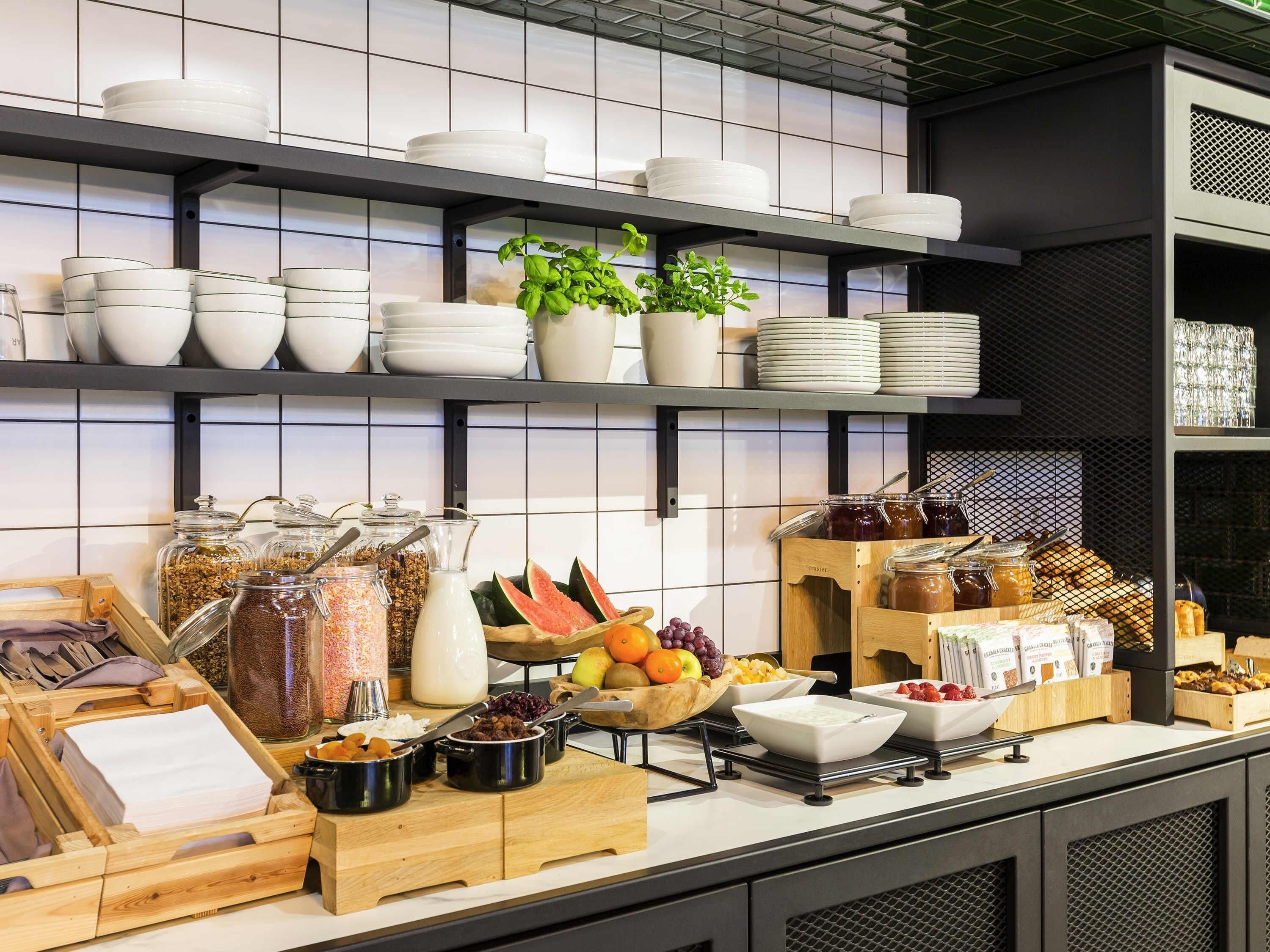 Uma área de cozinha com prateleiras contendo tigelas e pratos brancos, uma bancada com alimentos e uma planta em vaso.