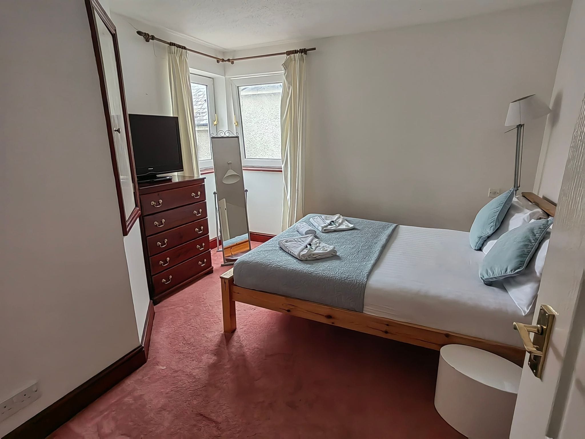 Quarto com cama, cómoda, televisão e janela com cortinas.