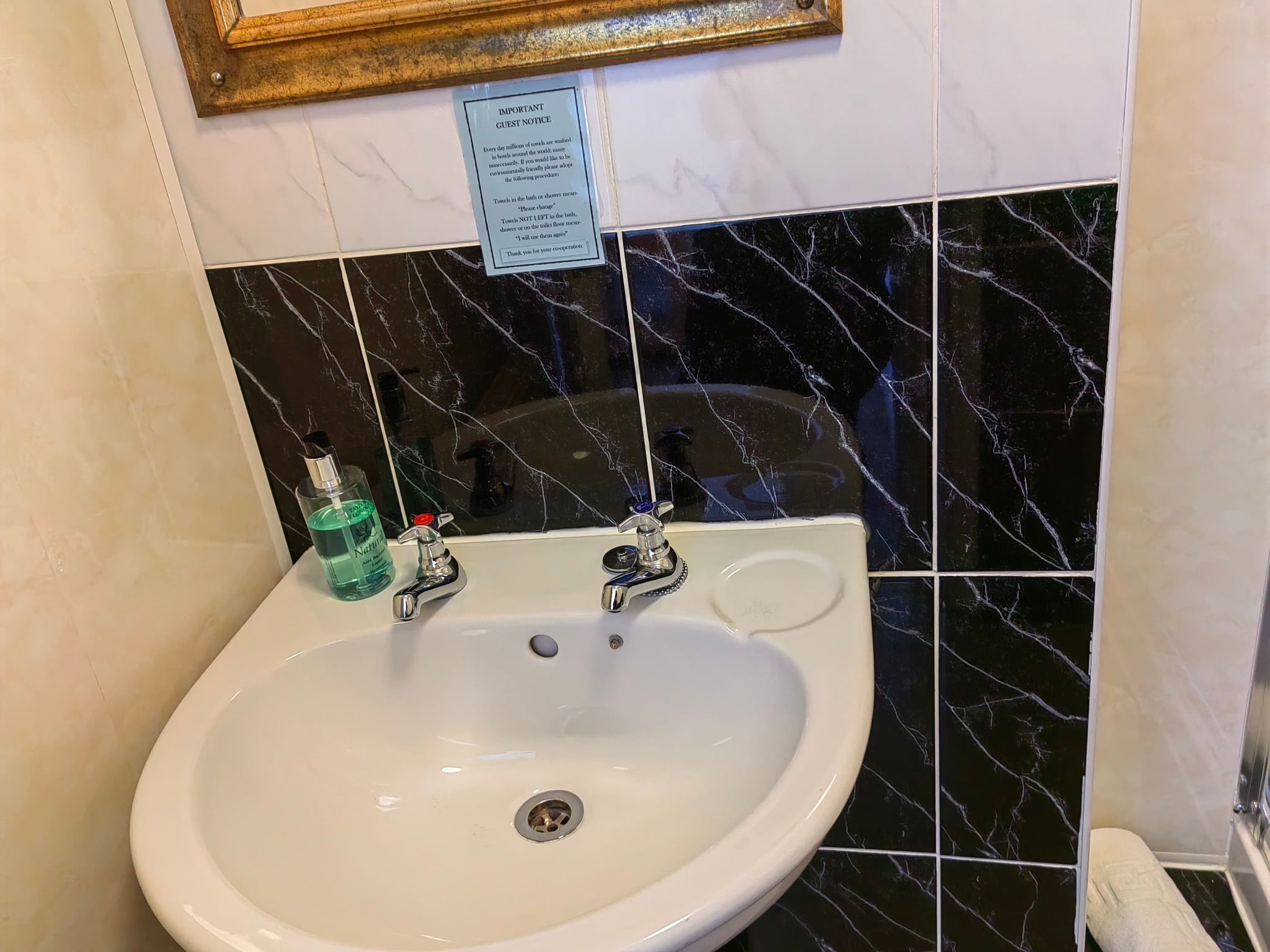 Uma pia de banheiro com uma bancada de mármore, um quadro emoldurado acima e um aviso para hóspedes na parede.