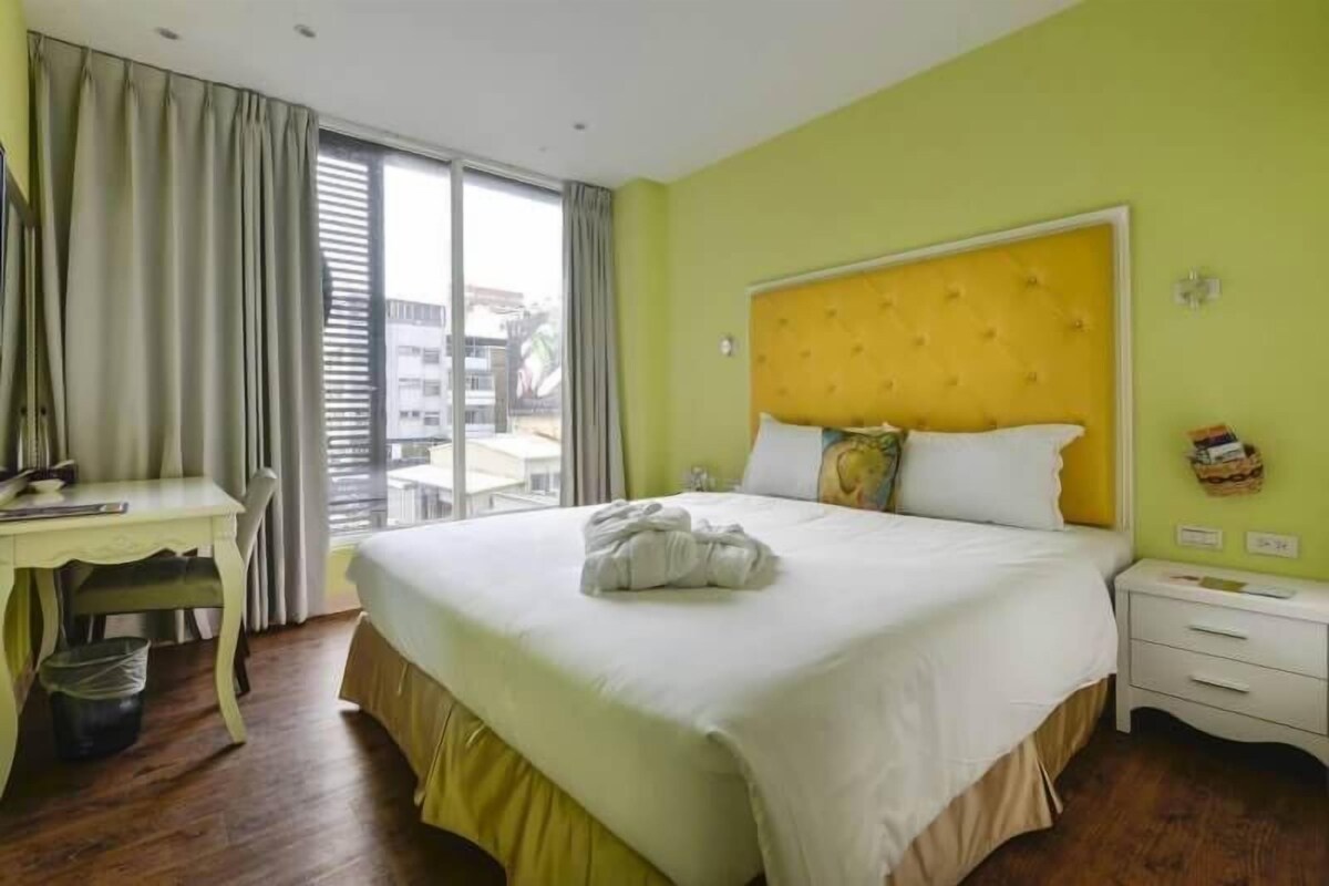 Quarto de hotel com cama, escrivaninha, cadeira e vista exterior.