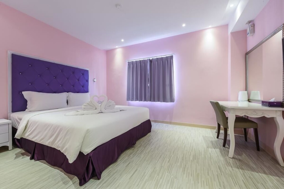 Quarto de hotel com cama, escrivaninha, cadeira, janela com cortinas e espelho.
