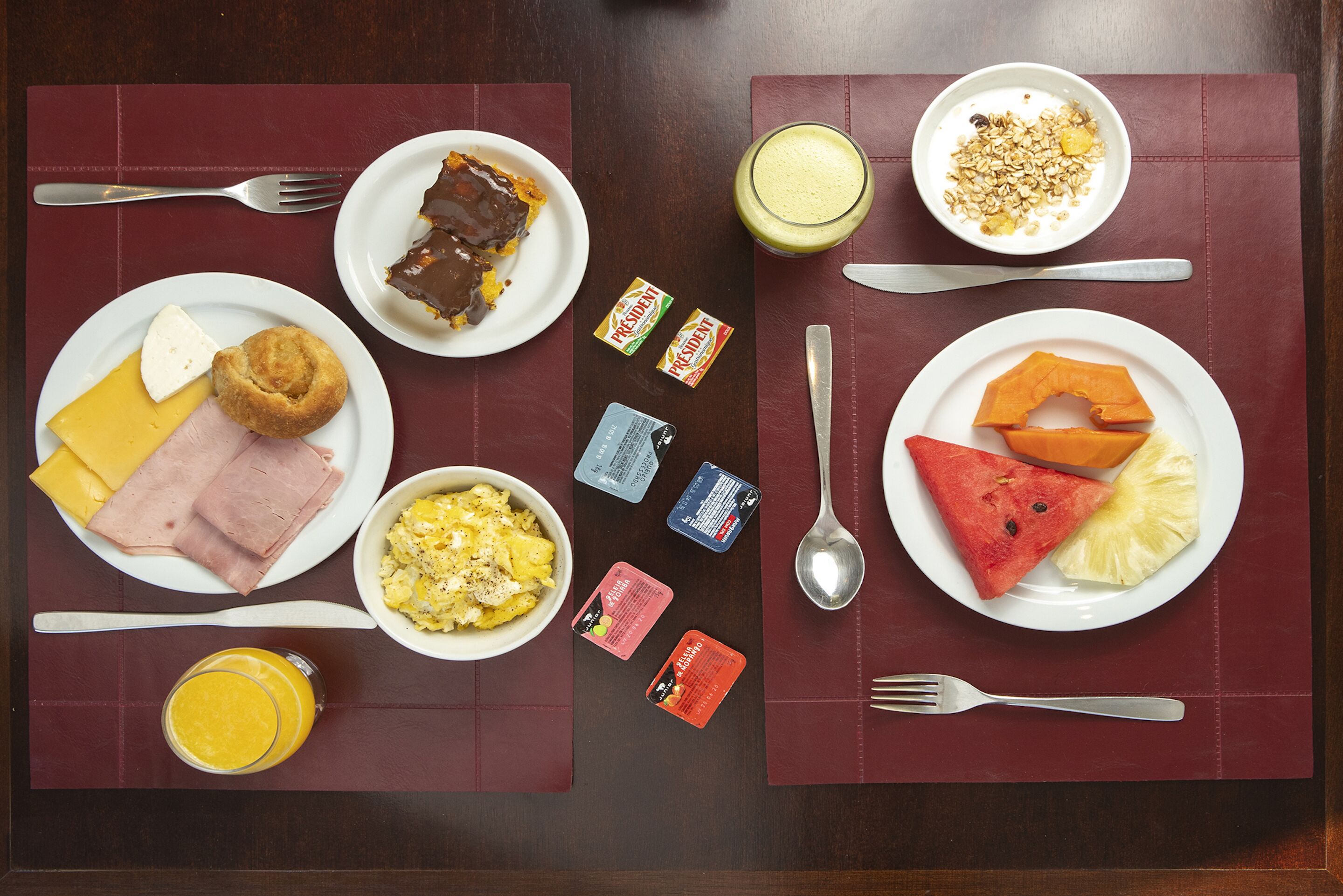 Uma mesa de café da manhã com pratos de comida, um copo de suco de laranja e um garfo.