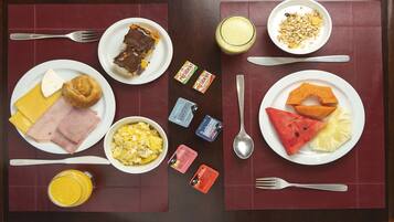 Uma mesa de café da manhã com pratos de comida, um copo de suco de laranja e um garfo.