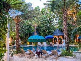Uma área à beira da piscina com espreguiçadeiras, guarda-sóis e um gazebo.