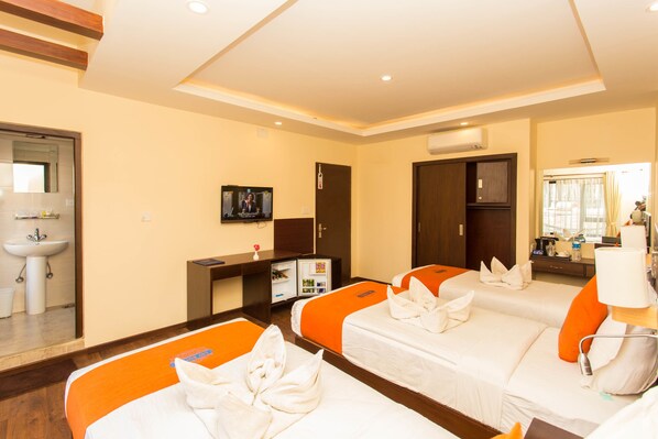 Quarto de hotel com duas camas, uma escrivaninha, televisão, mini-geladeira e banheiro com pia e espelho.
