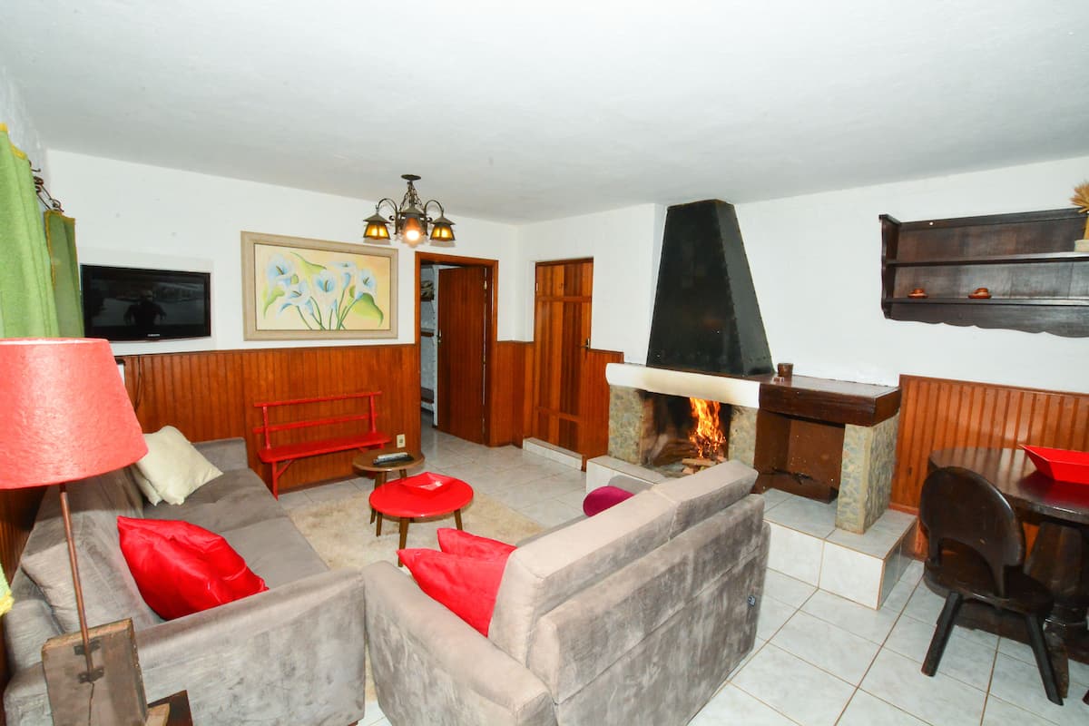 Uma sala de estar com lareira, um sofá, uma poltrona vermelha, uma televisão e um armário de madeira.