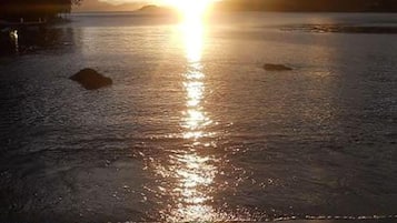 Um pôr do sol sobre um mar calmo, com uma praia arenosa e formações rochosas.