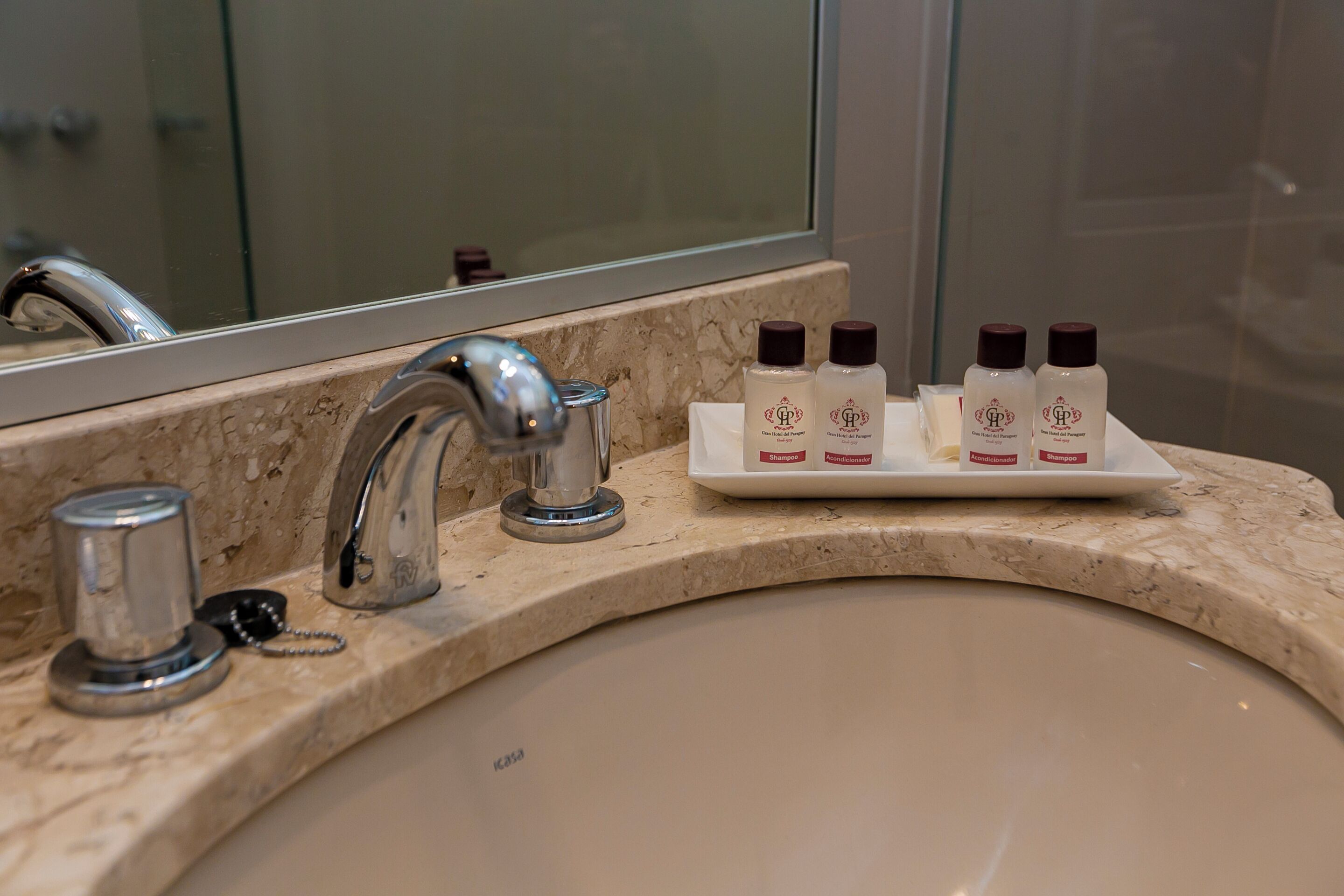 Uma pia de banheiro com torneira cromada, um saboneteira e um porta-bandeja com quatro frascos de shampoo e condicionador.
