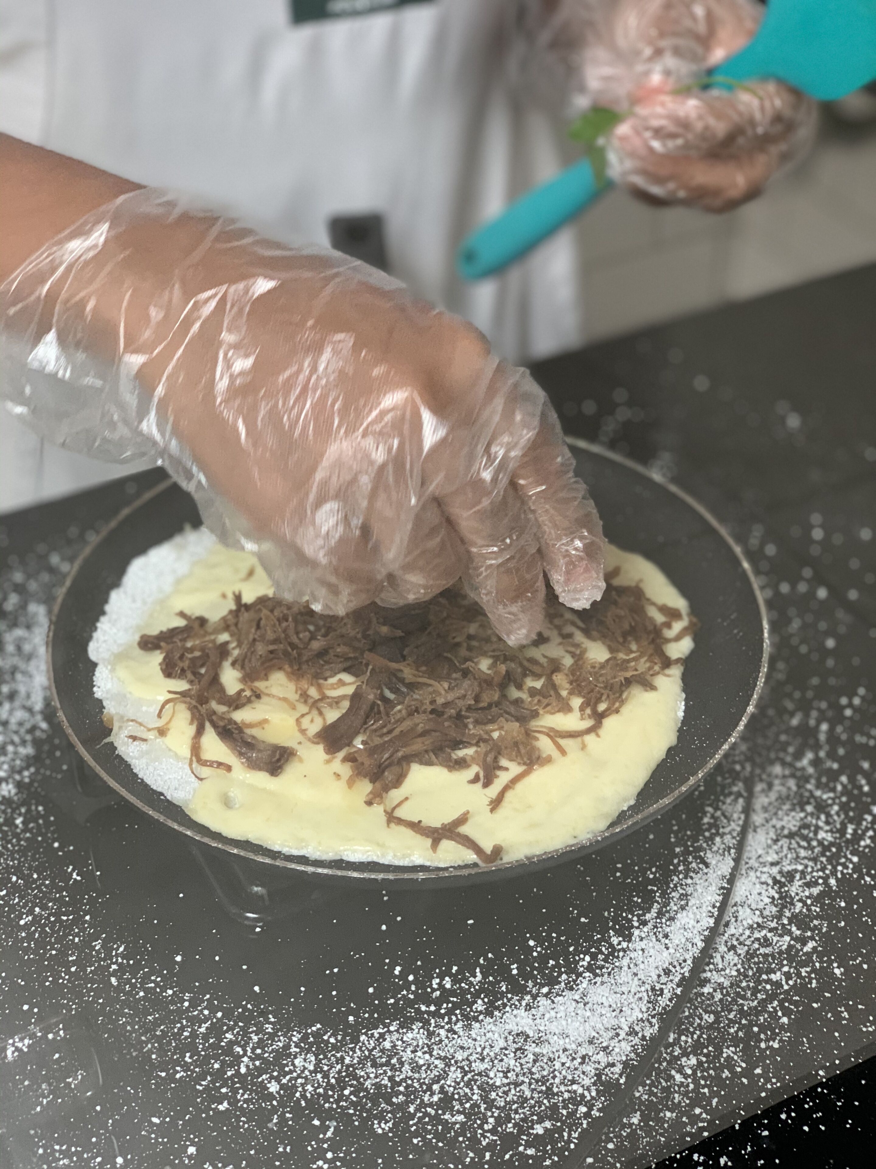 Alguém de luvas preparando comida em uma frigideira preta.