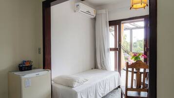 Quarto pequeno e limpo com cama, escrivaninha, cadeira e janela com cortinas.