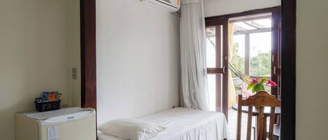 Quarto pequeno e limpo com cama, escrivaninha, cadeira e janela com cortinas.