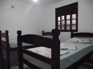 Quarto simples com duas camas de solteiro, janela com moldura de madeira e parede branca lisa.