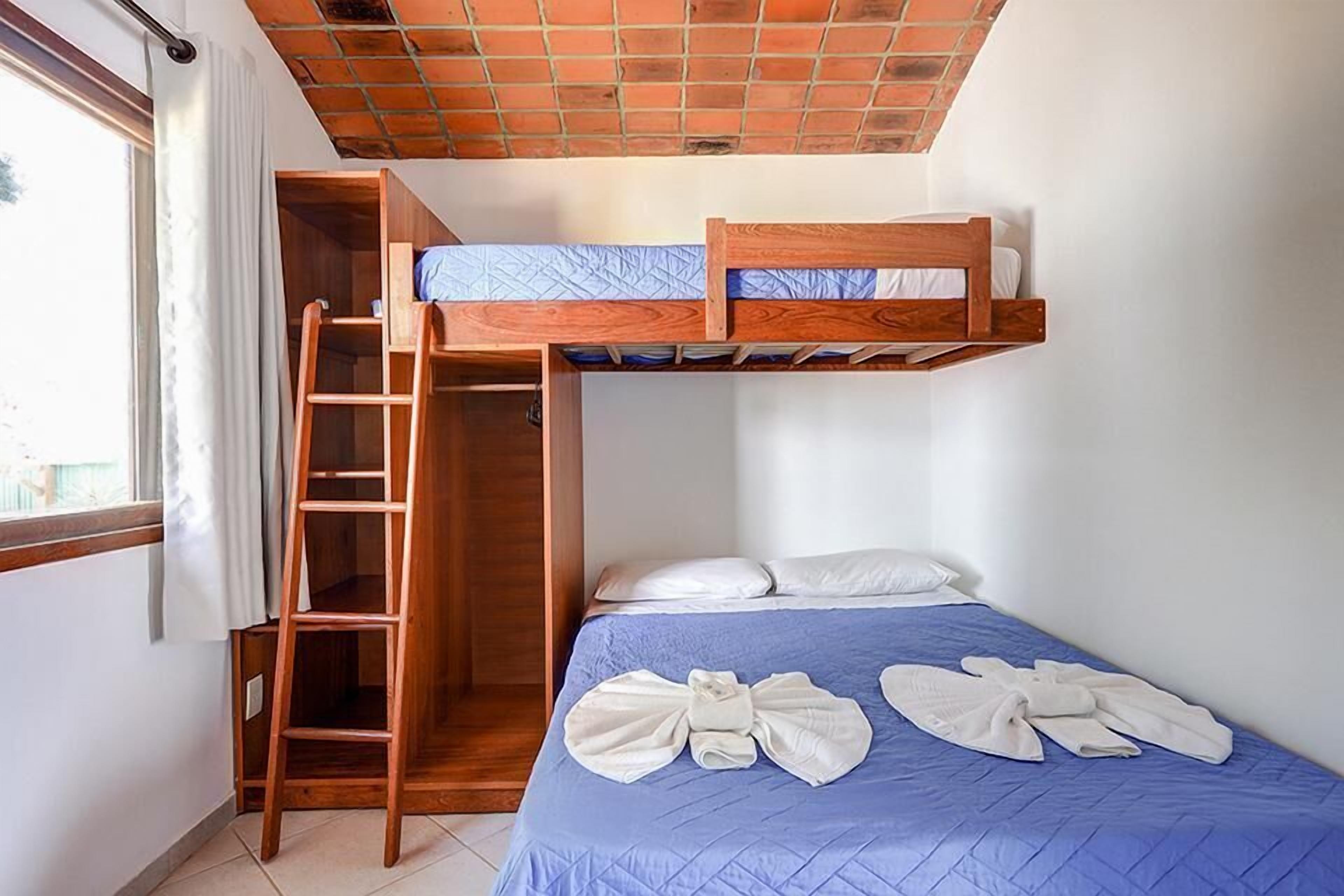 Uma cama beliche com escada, um cobre-leito azul e toalhas no chão.