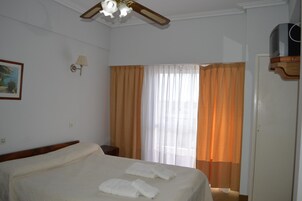 Quarto de hotel com cama, ventilador de teto, luminária na parede e cortinas.
