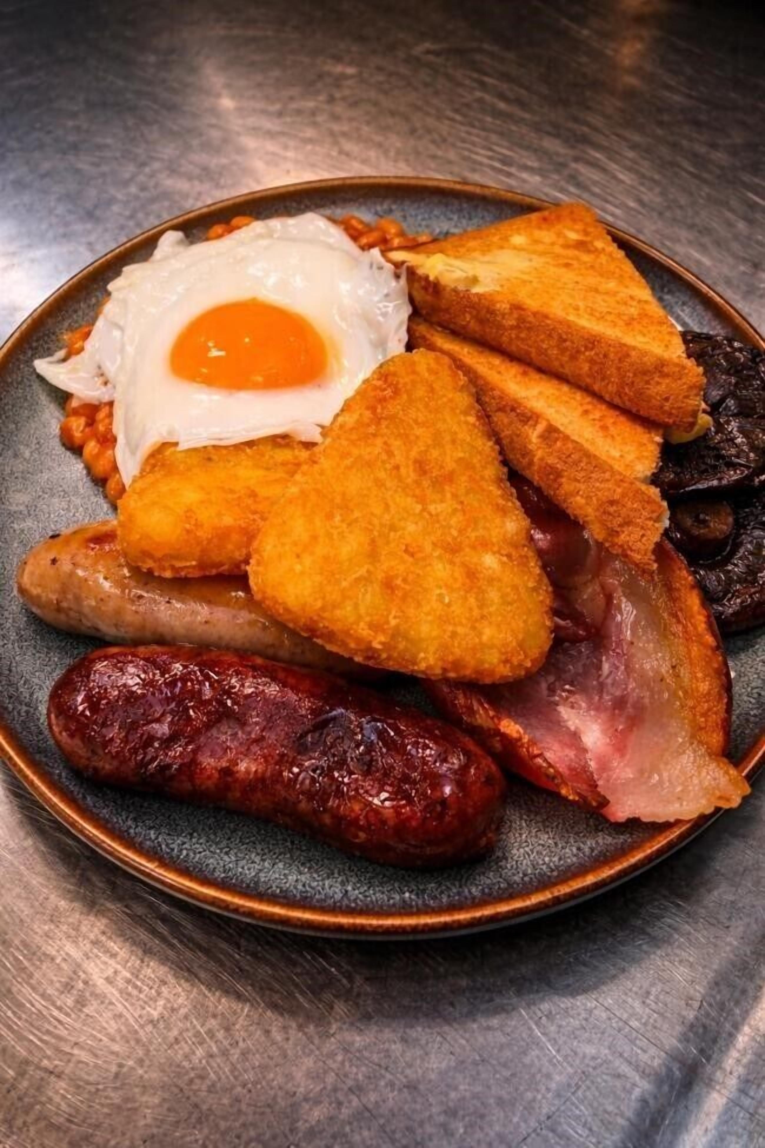 Um prato de comida de café da manhã com torradas, ovos, feijão, salsichas e bacon.