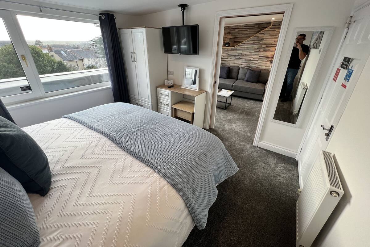 Quarto com cama, escrivaninha, televisão e vista para o exterior.