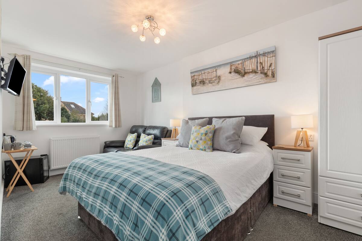 Quarto com cama, escrivaninha, cadeira, televisão e janela com vista.