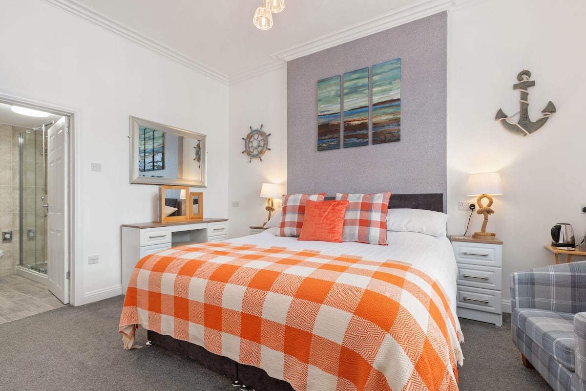 Quarto com uma cama grande, cômoda, mesa de cabeceira, cadeira e um quadro na parede.